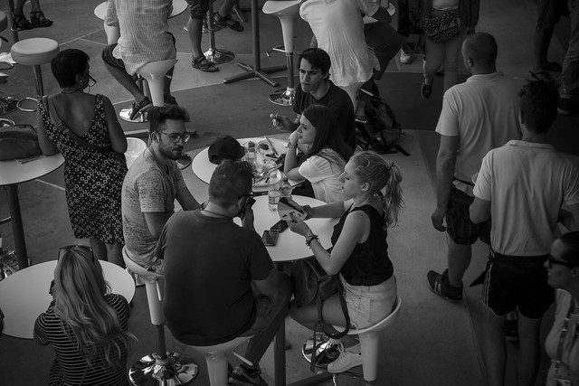 Candid Milan outdoor café scene: groups gathered around round white tables on white bar stools